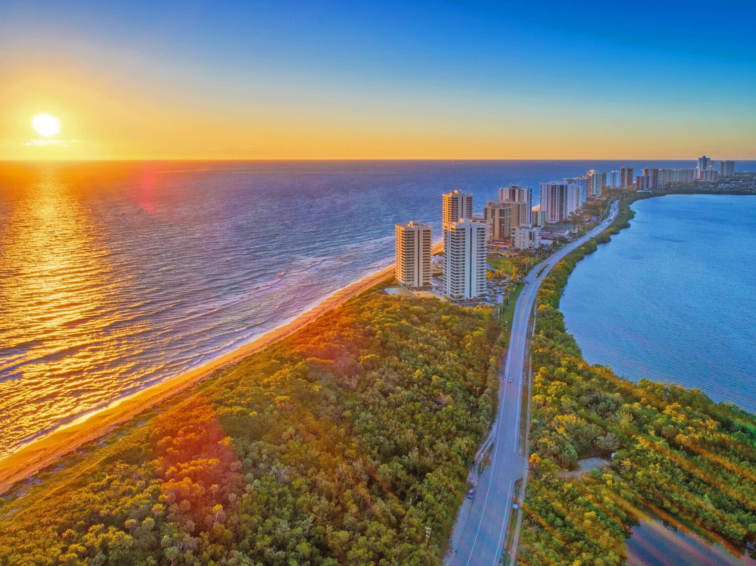 A beautiful aerial shot of the ocean during sunset with views of buildings and greeneries.