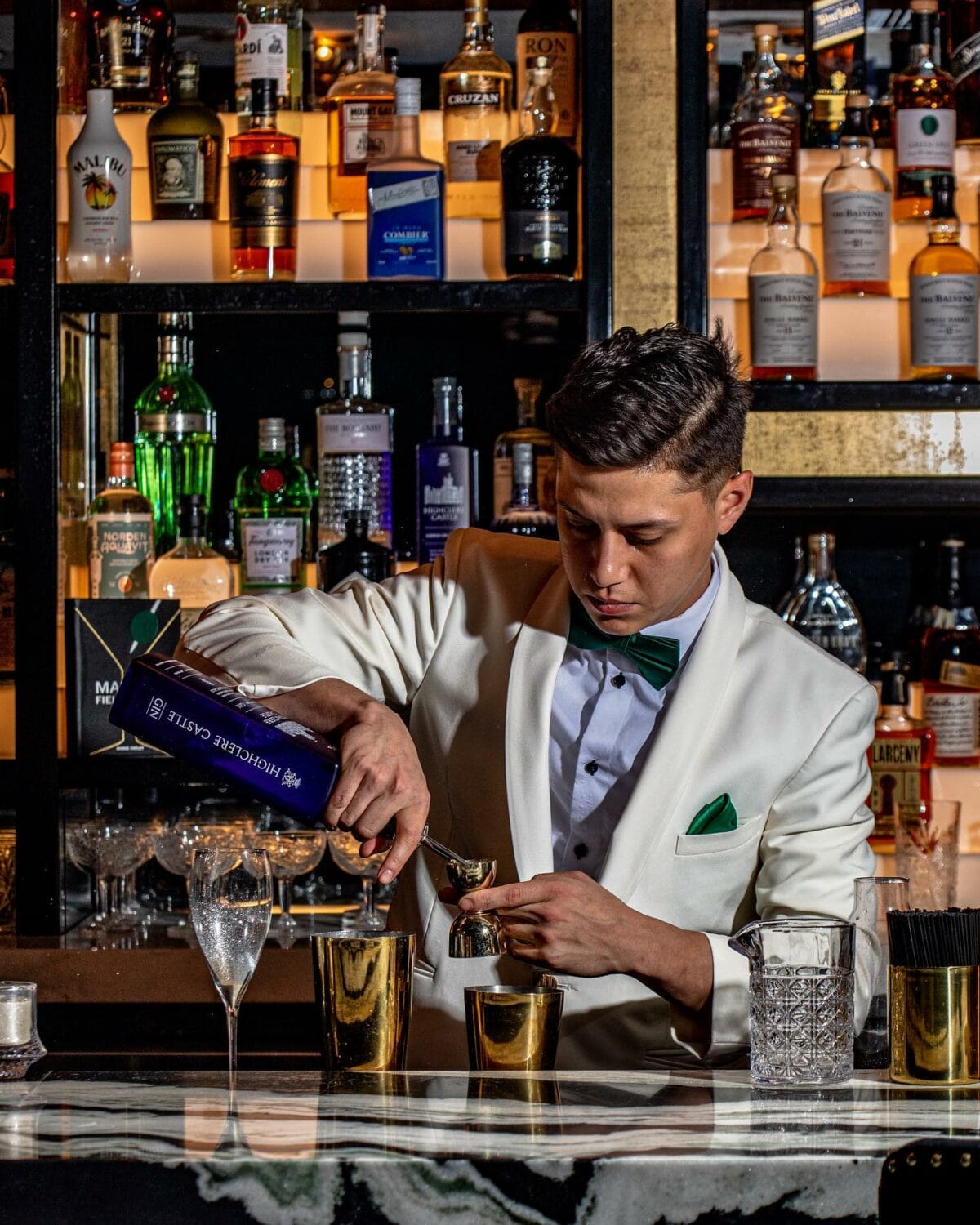 A bartender in a stylish suit at the bar, making a hand crafted cocktail