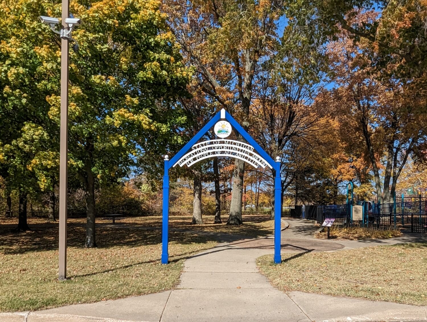 a bright blue park entrance sign over a pathway leading to a childrens playground indicating a community recreational area