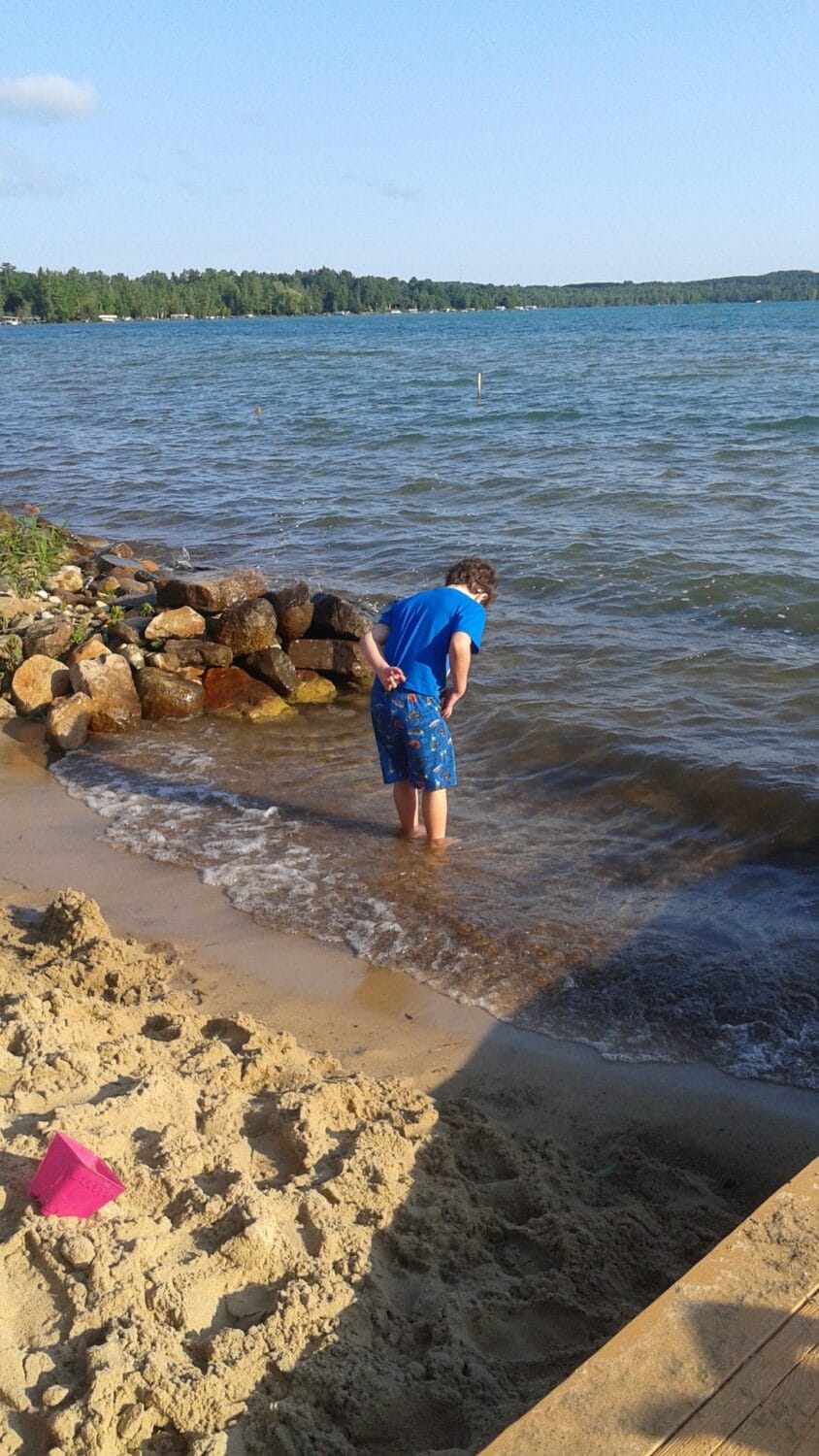 a child in blue shorts plays at the edge of a clear lake with a sandy beach