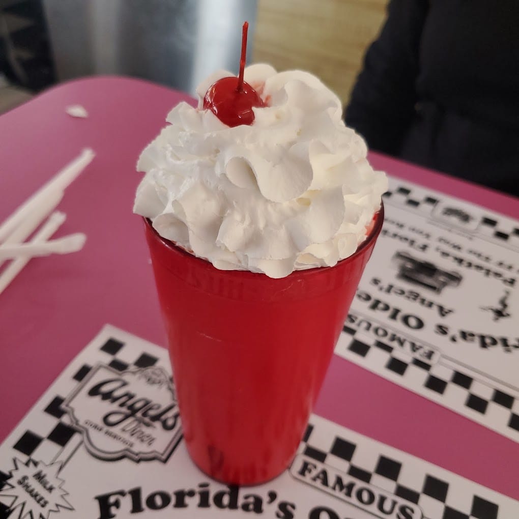 a classic red milkshake topped with whipped cream and a cherry set on a pink diner table