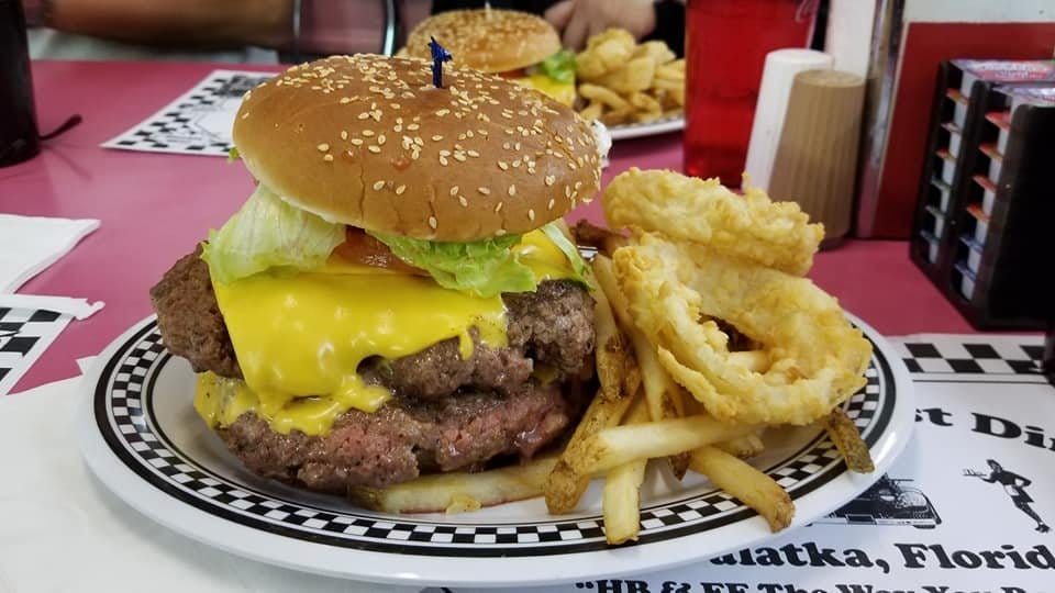 a close up of a diner meal with a double cheeseburger onion rings and fries served on a checkered tablecloth
