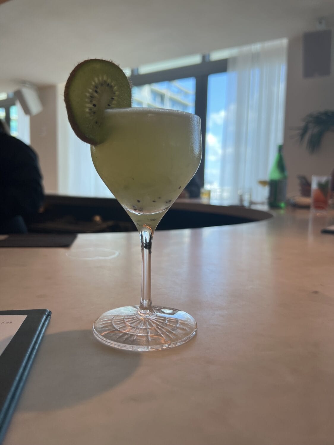 a cocktail drink served in a tall glass with a sliced kiwi