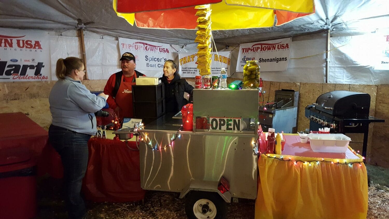 a cozy food stall adorned with festive lights serving customers with a sign saying open under a tent