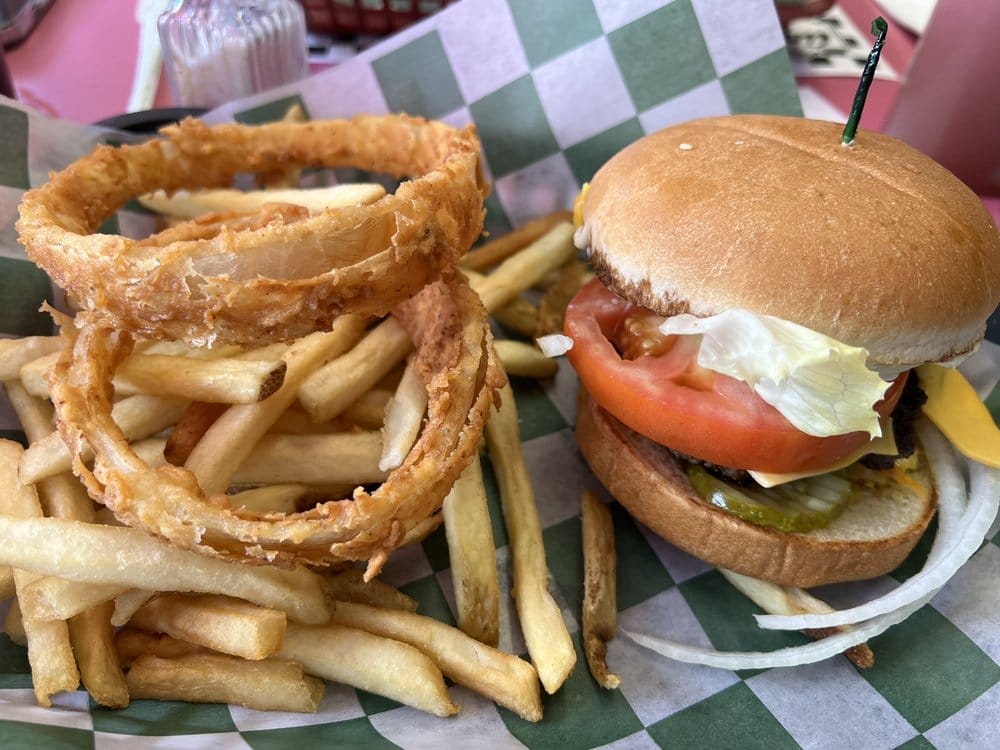 a diner meal showcasing a cheeseburger with lettuce and tomato accompanied by onion rings and fries presented on checkered paper