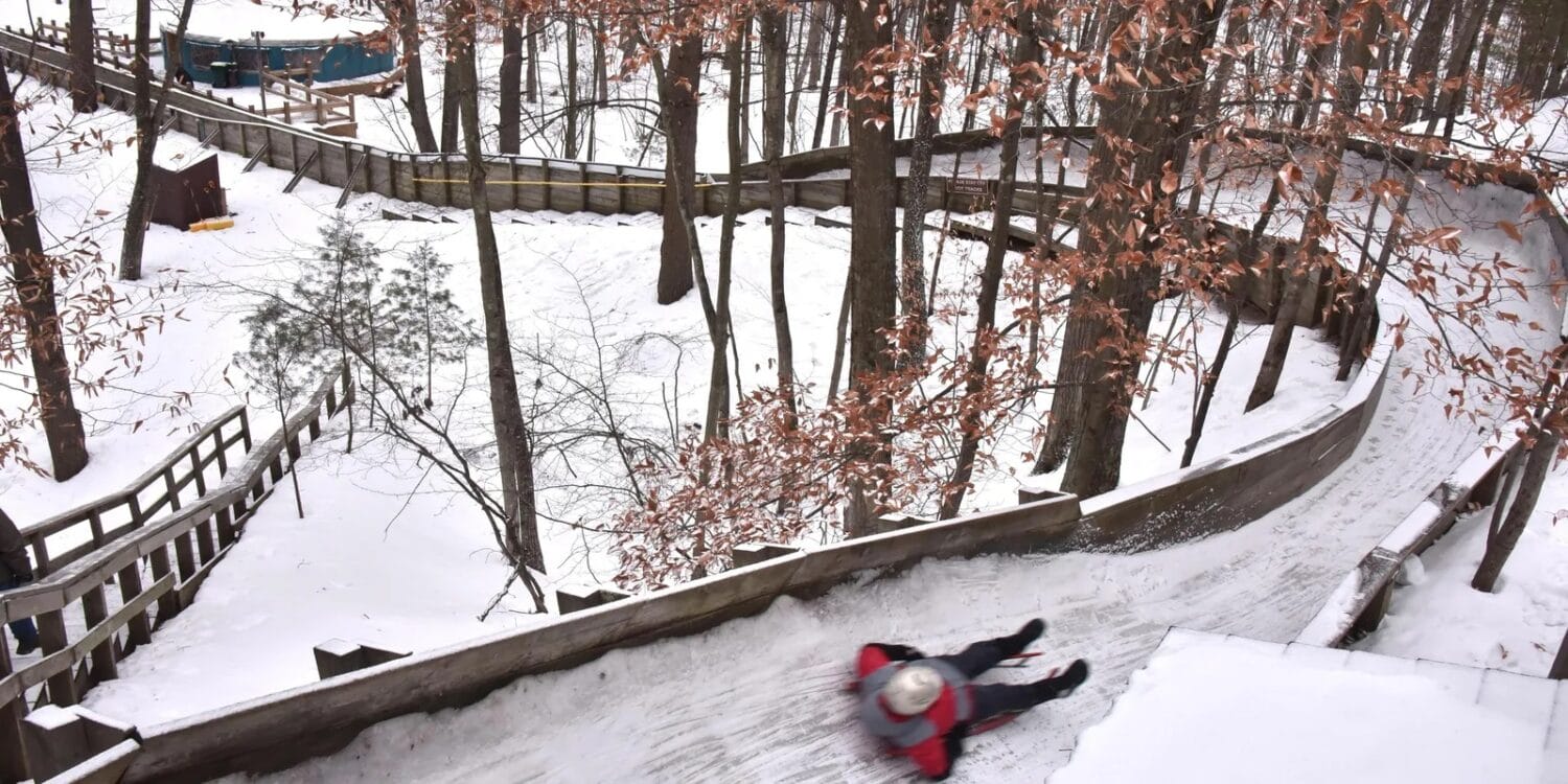 a dynamic action shot capturing a person sledding down a snowy luge track with a blurred motion effect emphasizing the speed and excitement of the ride