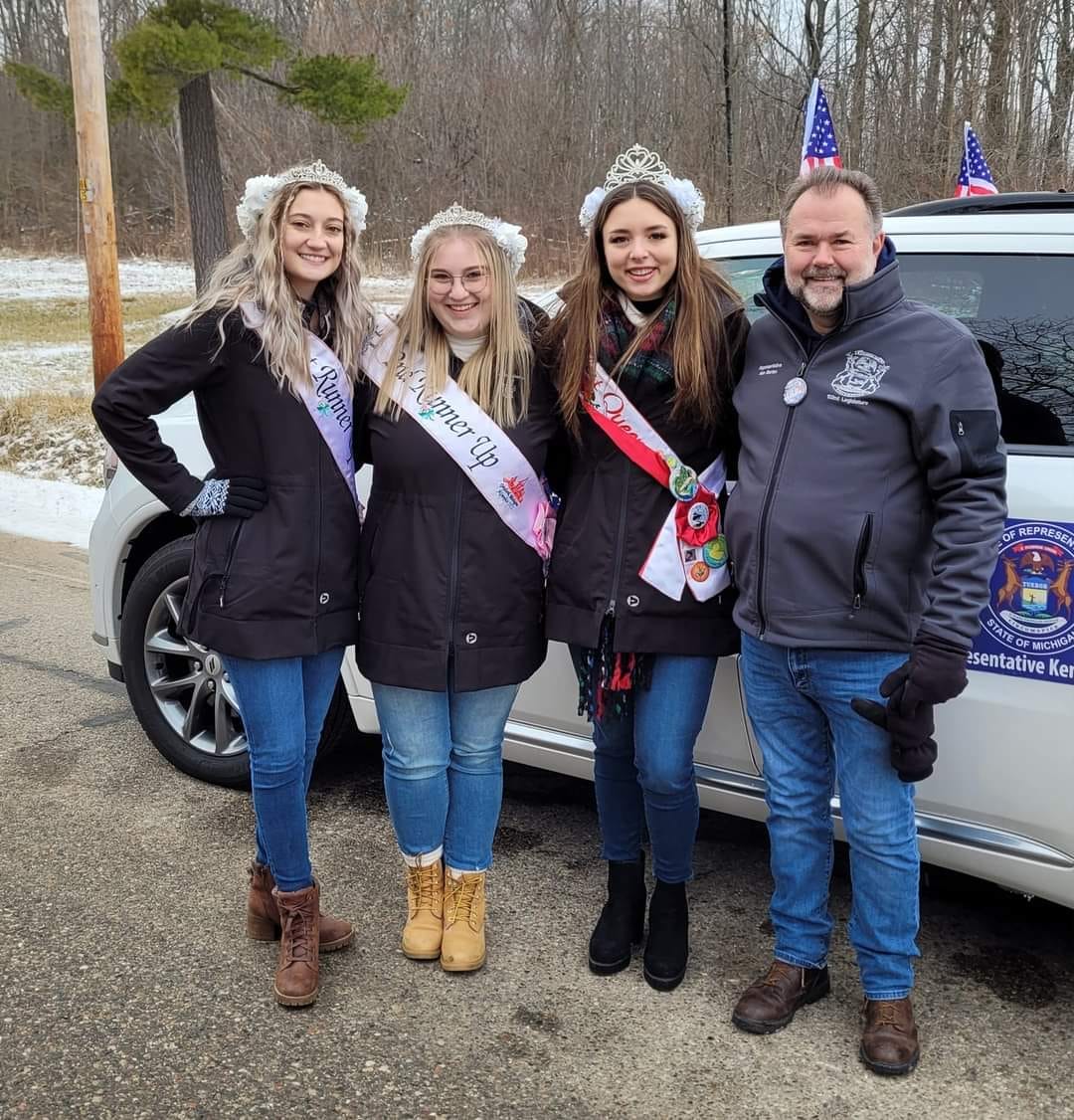 a group of three young women and a man with the women wearing pageant sashes and tiaras