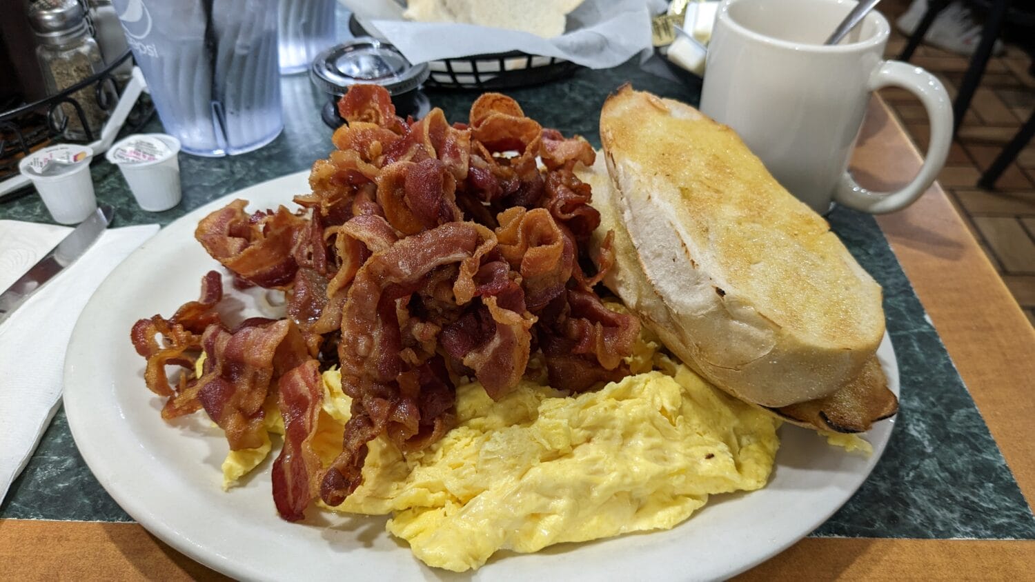 a hearty american breakfast plate piled high with bacon eggs and toast served on a diner table