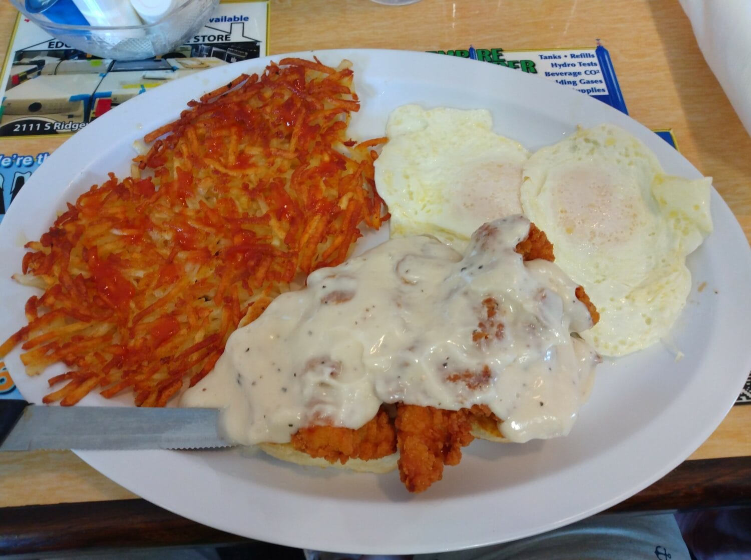 a hearty breakfast plate with crispy hash browns fried eggs and chicken fried steak topped with gravy