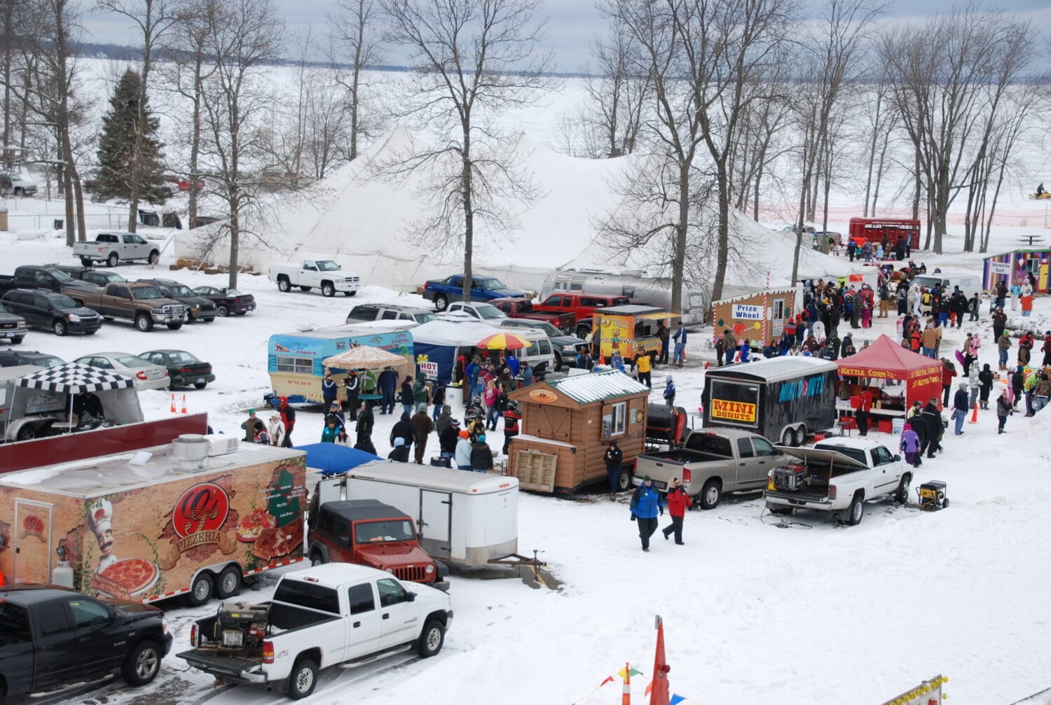 a lively winter carnival scene with various food trucks vendor stalls and a crowd of visitors on a snowy day