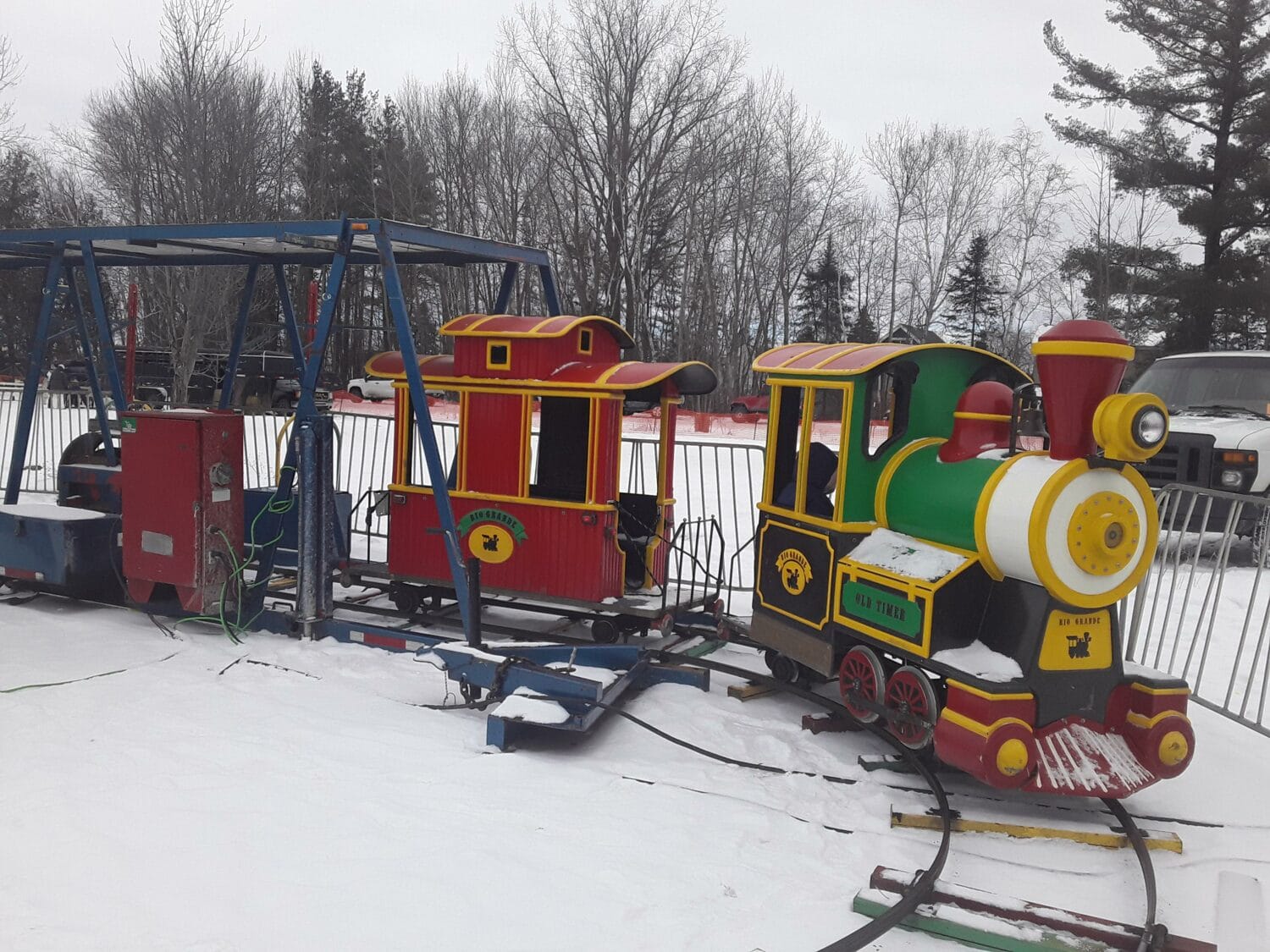 a miniature train ride for children set up on snowy terrain with bare trees in the background