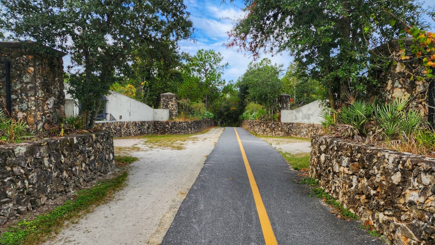 a paved trail leading between old stone pillars and lush greenery suggesting a gateway to a serene natural area