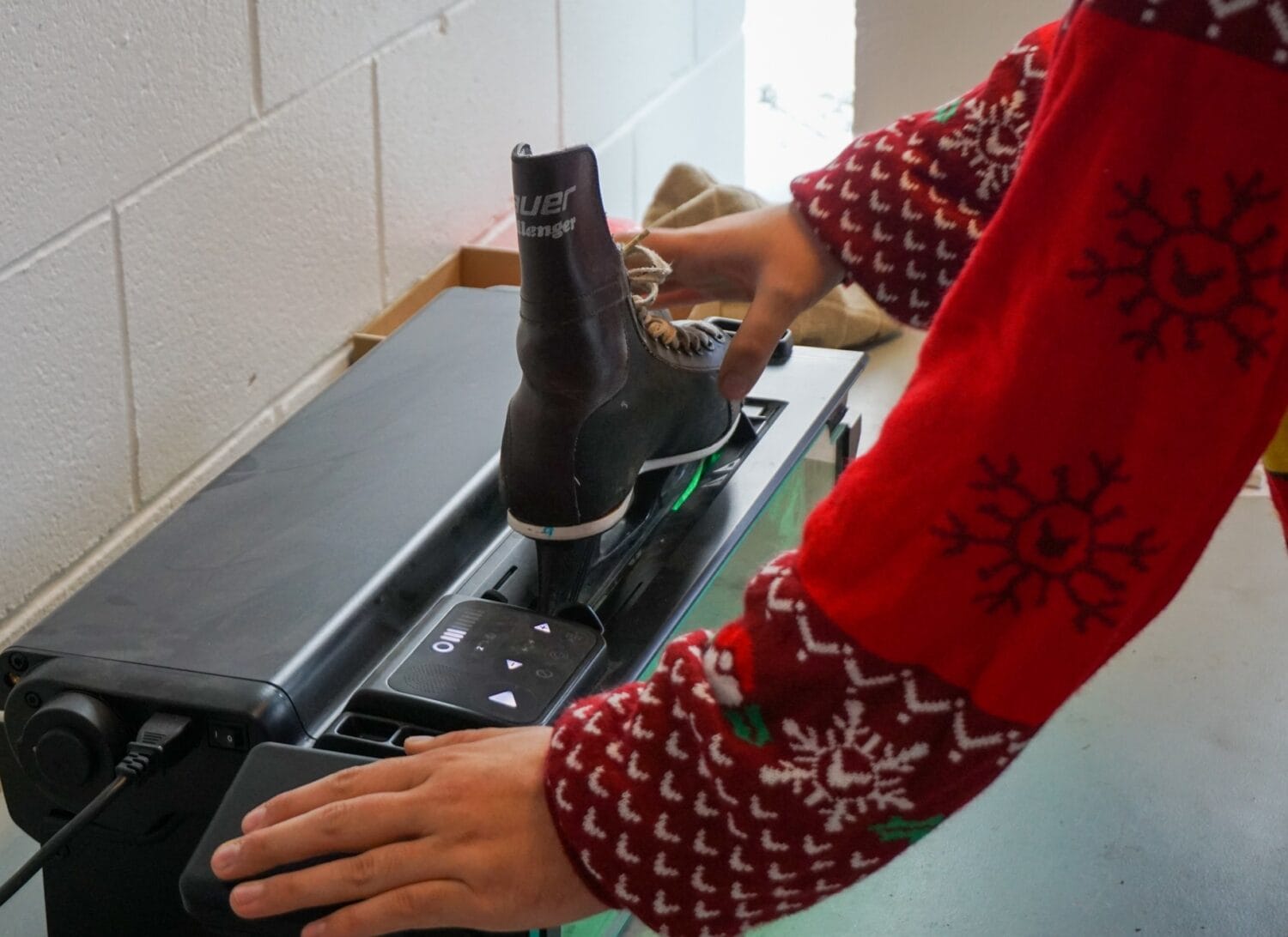 a person wearing a festive sweater prepares to sharpen an ice skate on a modern machine