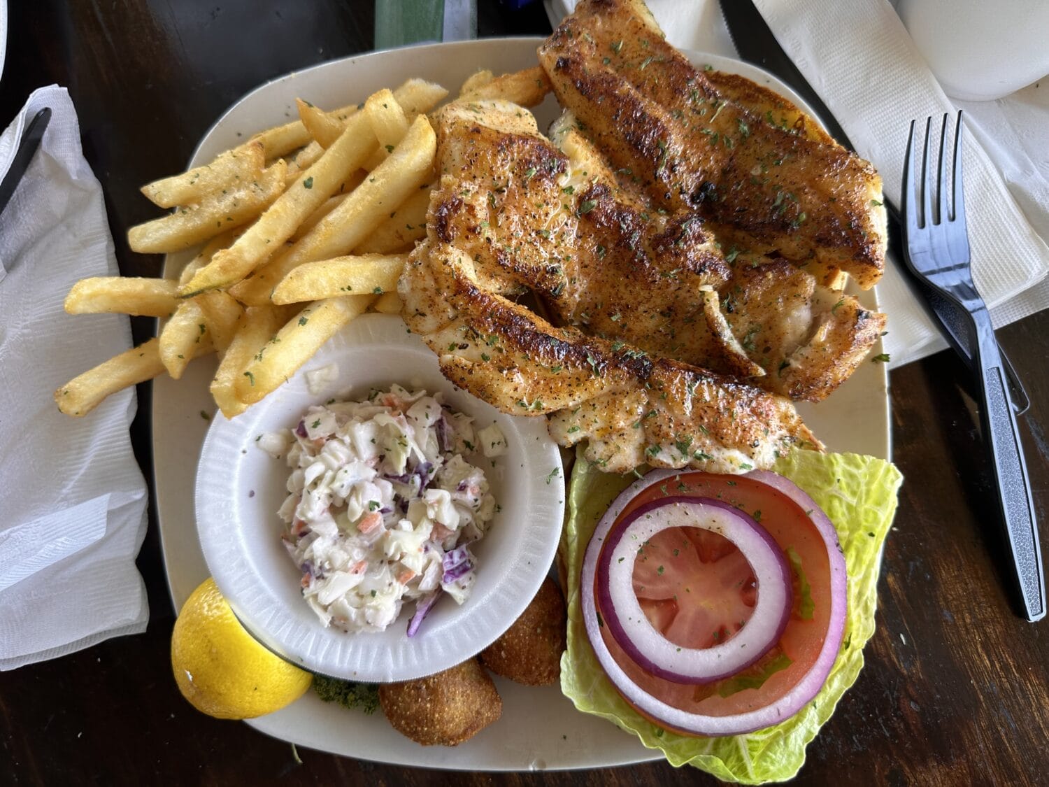 a plate with grilled fish seasoned fries coleslaw and fresh lemon served on a wooden table