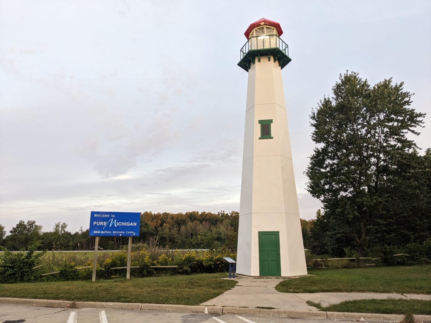 a quaint lighthouse structure with a green door set in a landscaped area with a welcome to pure michigan sign