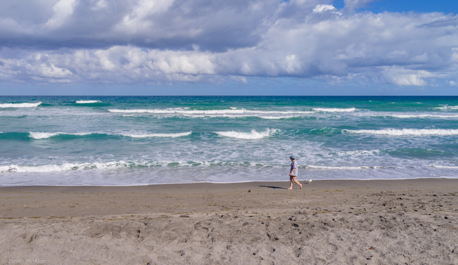 a serene beach scene with a person walking along the shoreline under a sky scattered with cumulus clouds