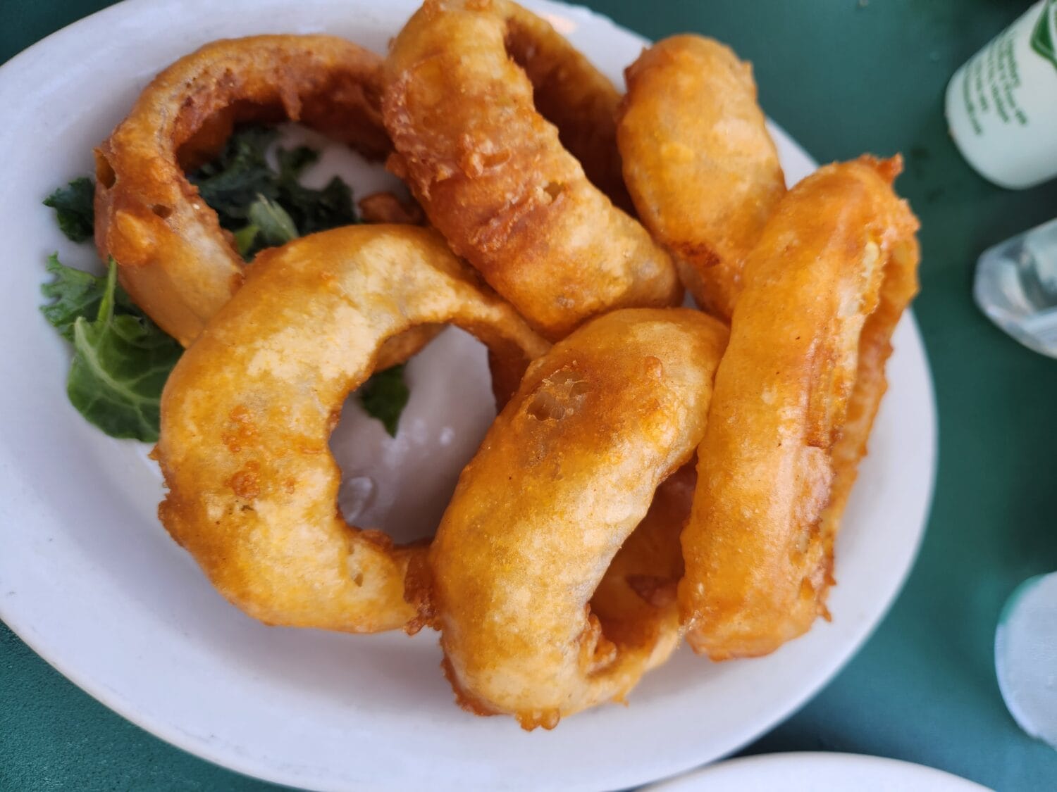 a serving of golden brown onion rings on a bed of greens with a dipping sauce