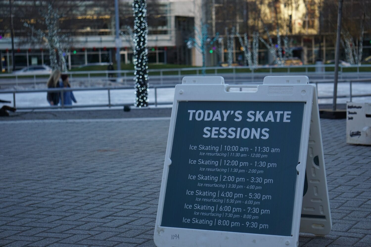 a sign detailing ice skating session times stands in front of rosa parks circle ice rink
