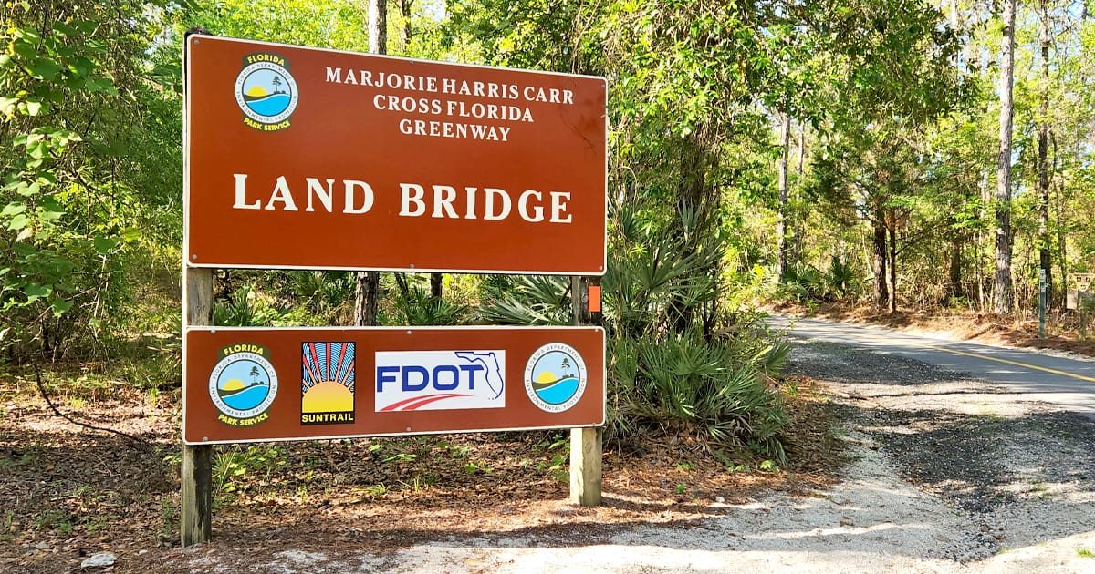 A sign for the The Landbridge Trailhead which marks the entrance to a forested trail.
