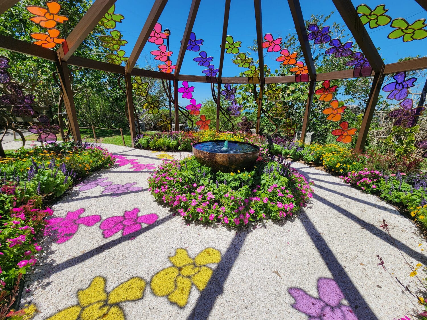 a small fountain inside an open structure surrounded by colorful flowers