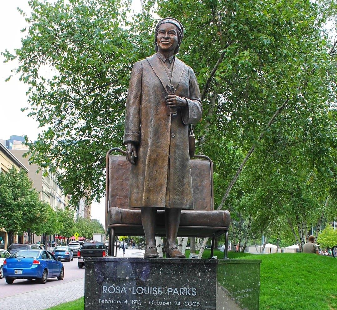 a statue of rosa parks standing proudly on a seat, with an informative plaque detailing her significant contribution to the civil rights movement