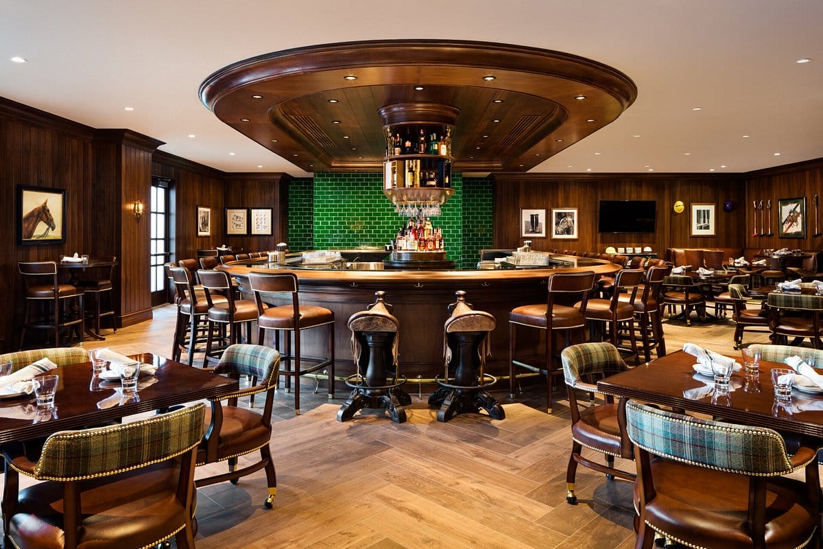 a traditional bar setting with a dark wood circular bar leather stools and green tile accents