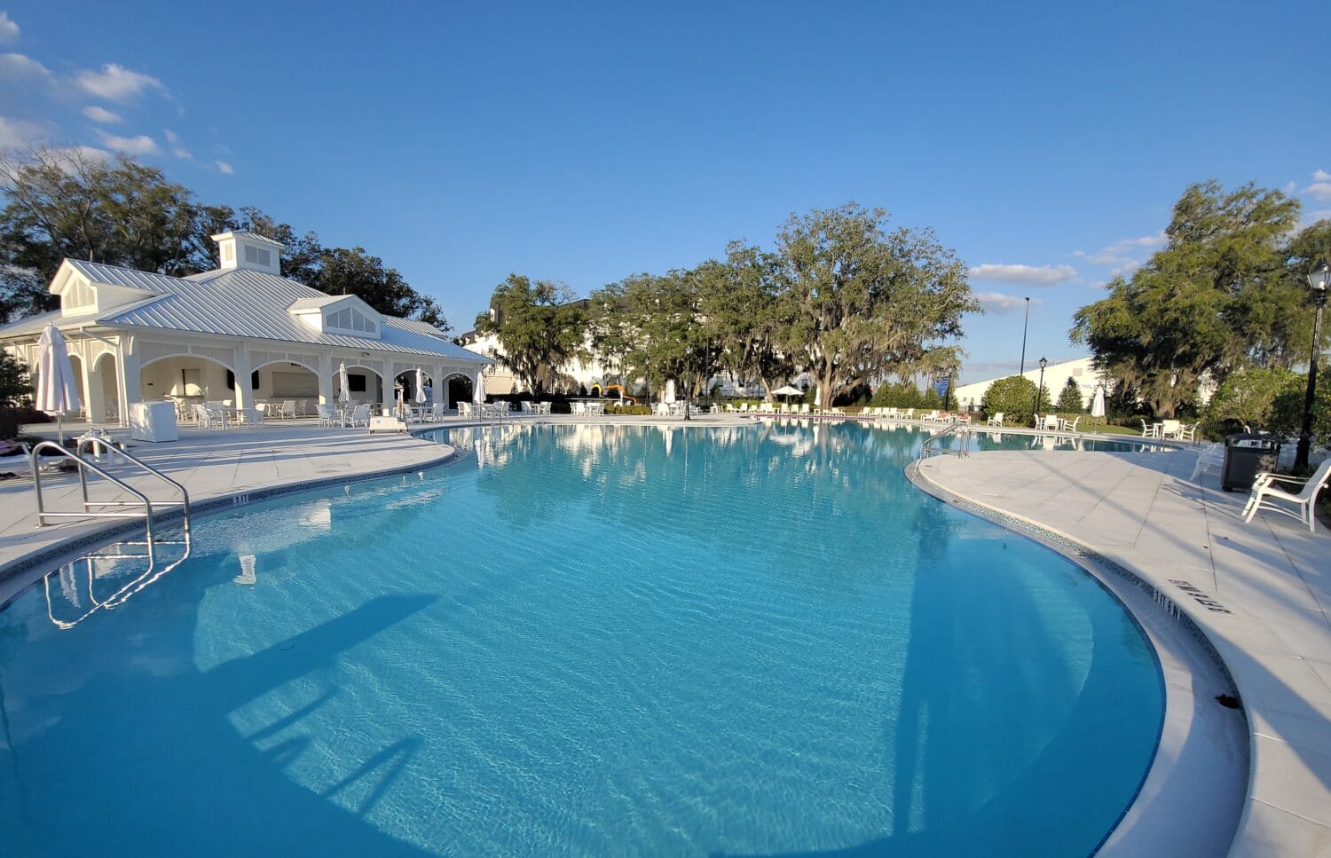 a tranquil outdoor swimming pool surrounded by white architecture and mature trees under a clear sky