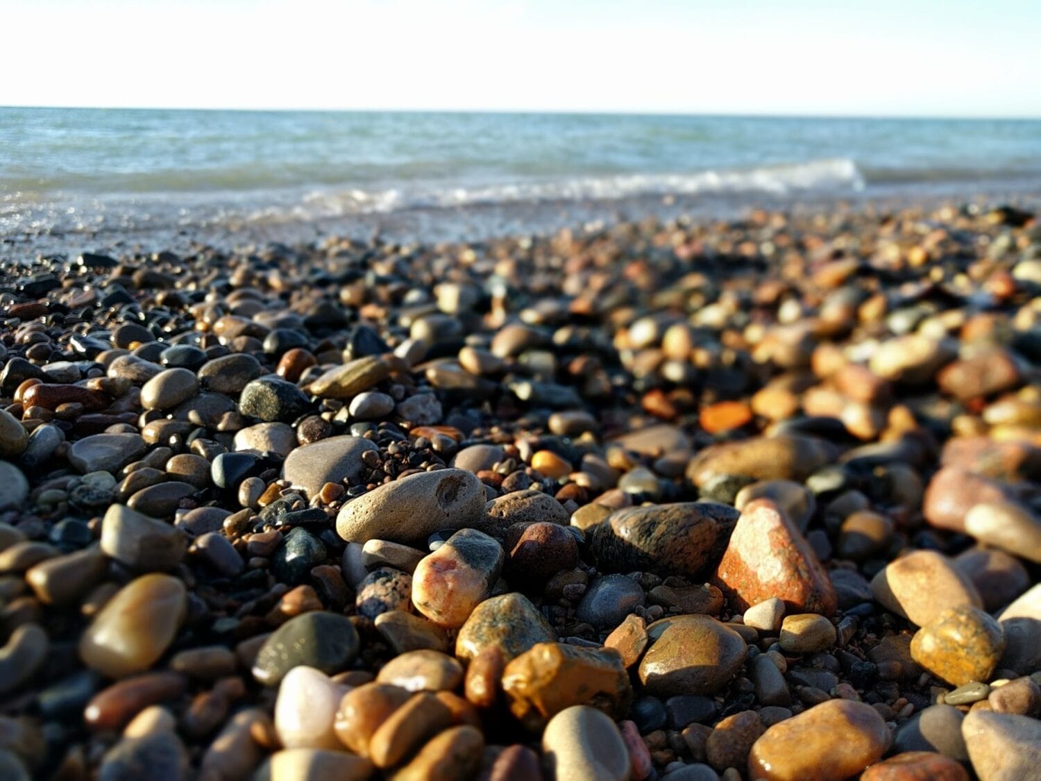 a vast collection of rounded pebbles blankets the shore with waves softly breaking in the background
