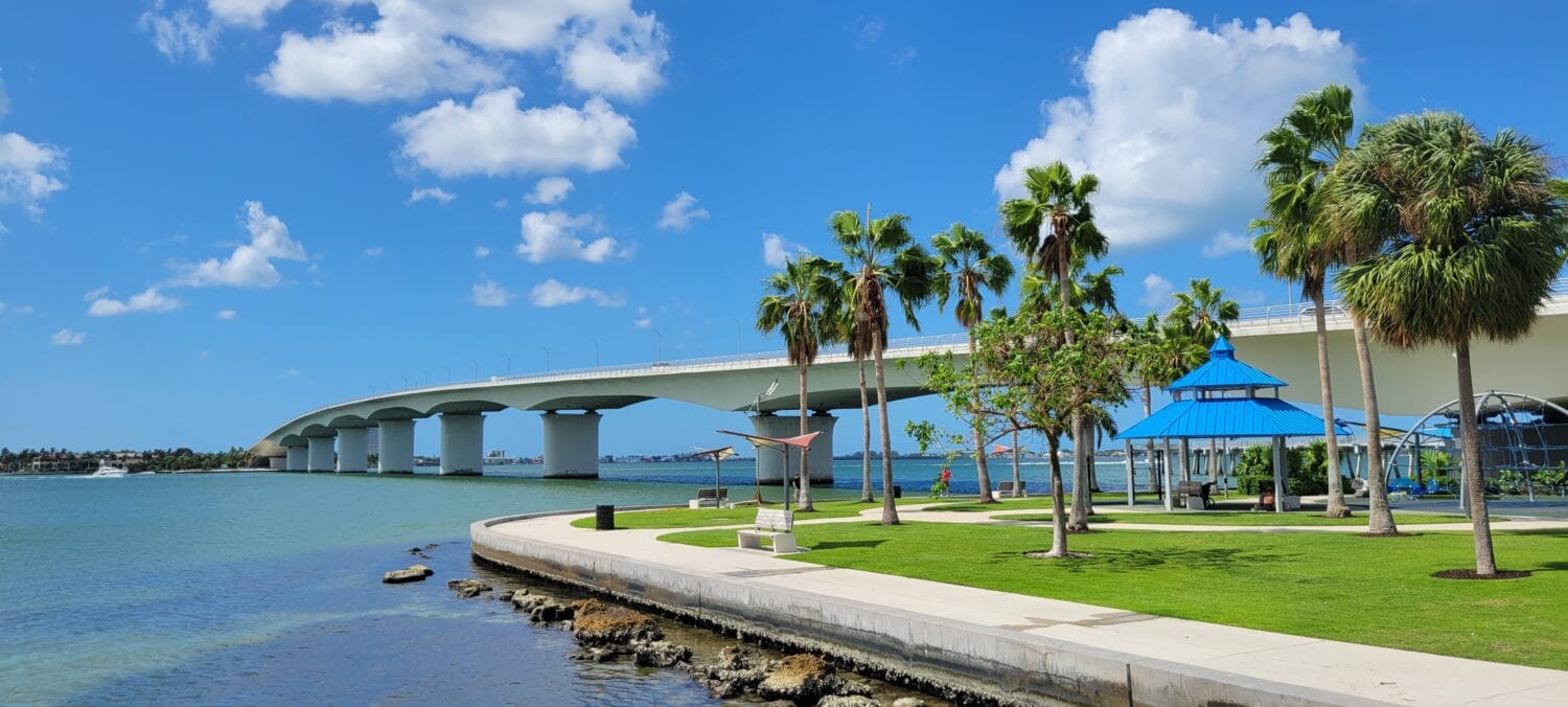 a view of a bridge from a paark surrounded by waters during a clear day