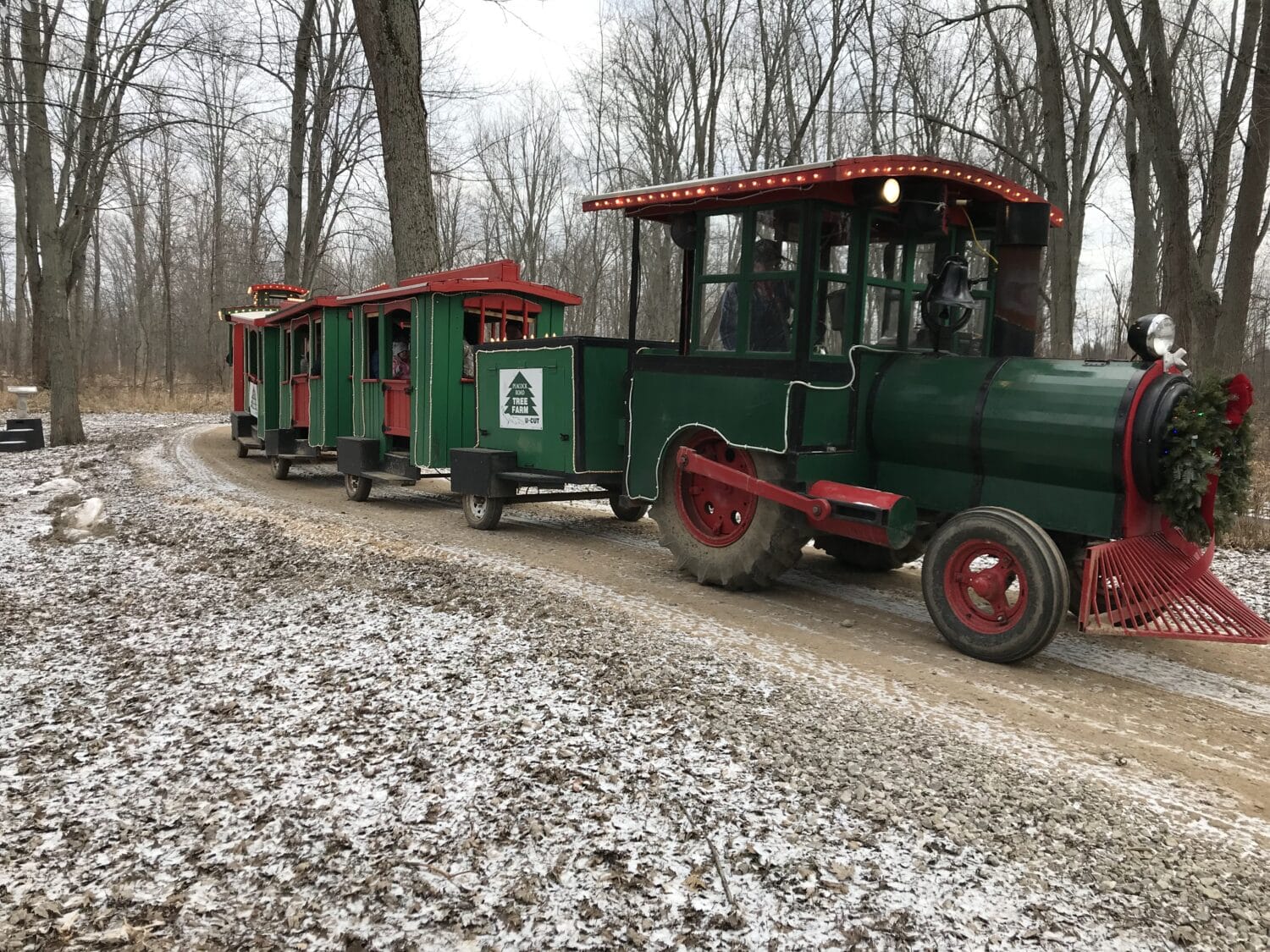 a vintage looking green and red train adorned with wreaths and holiday decorations waits to take visitors on a scenic ride through the winter woods