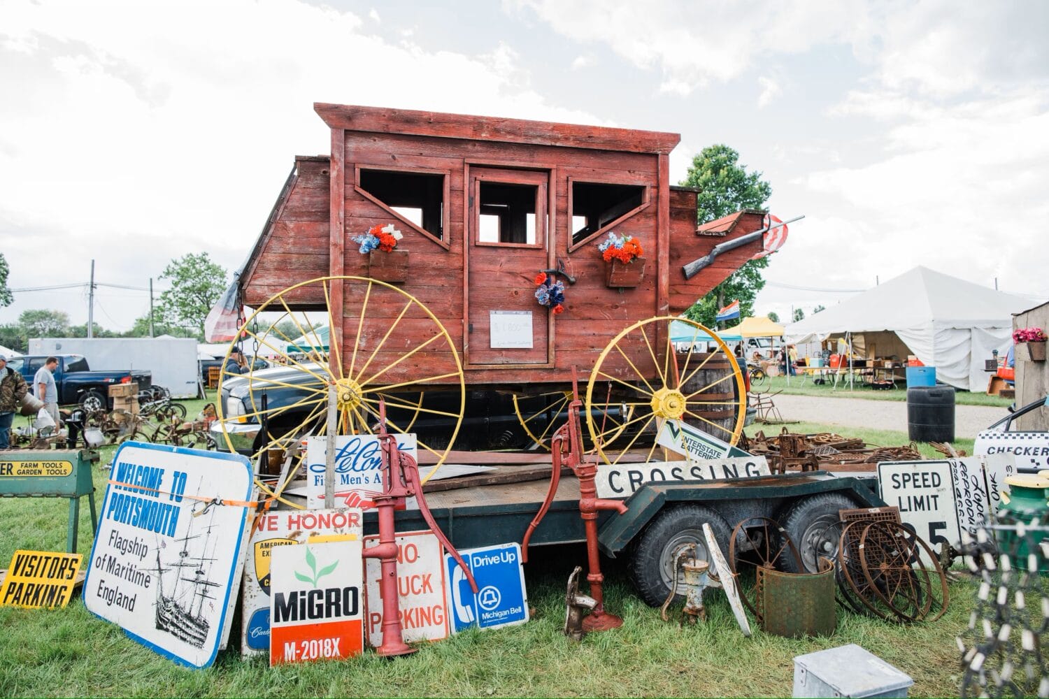a whimsical vintage caboose adorned with flowers and surrounded by assorted antique signs and farm equipment on display