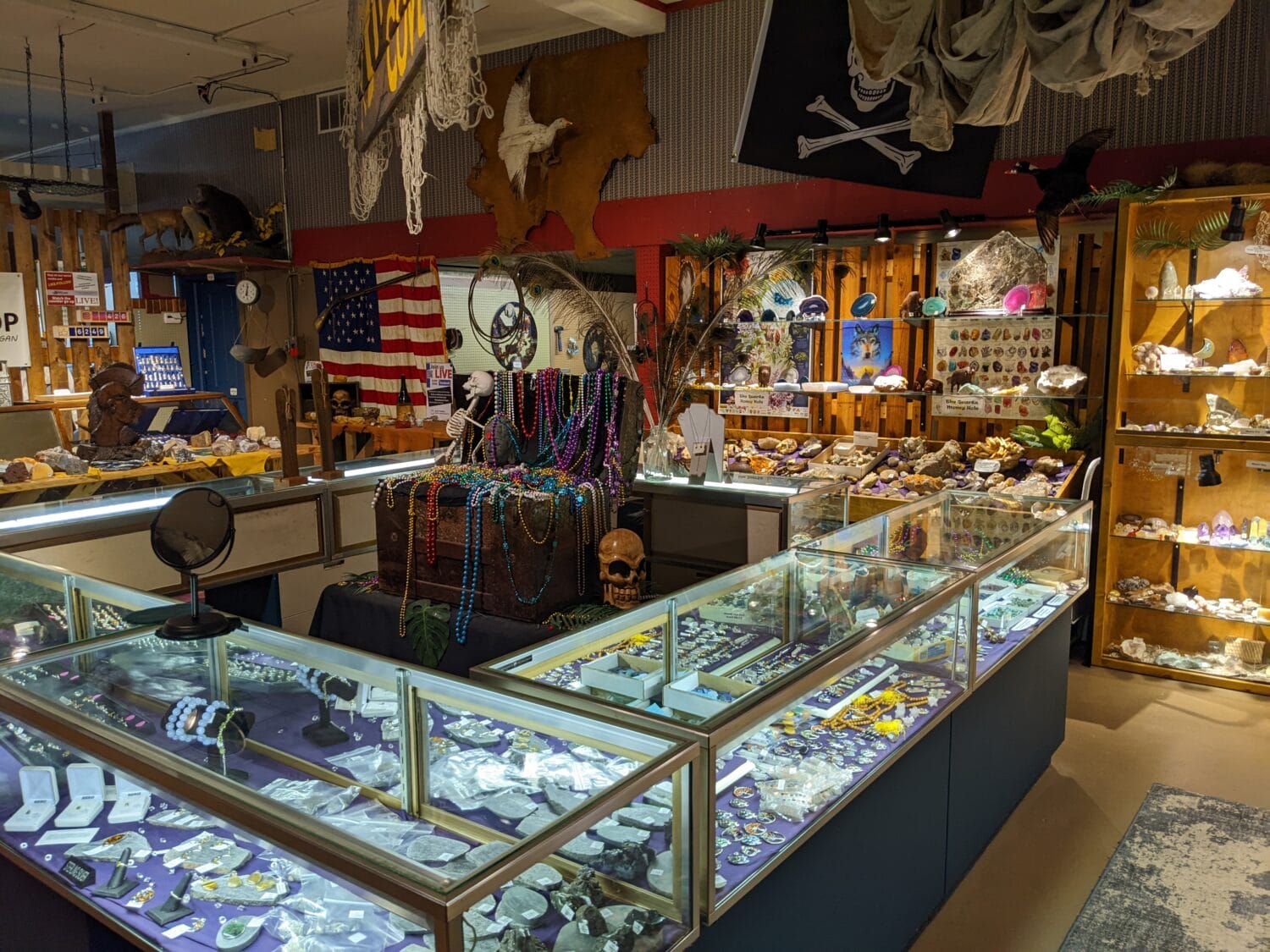 a wide view of a rock shops interior with various gemstones jewelry and decorative items with american flags and a pirate flag in the background