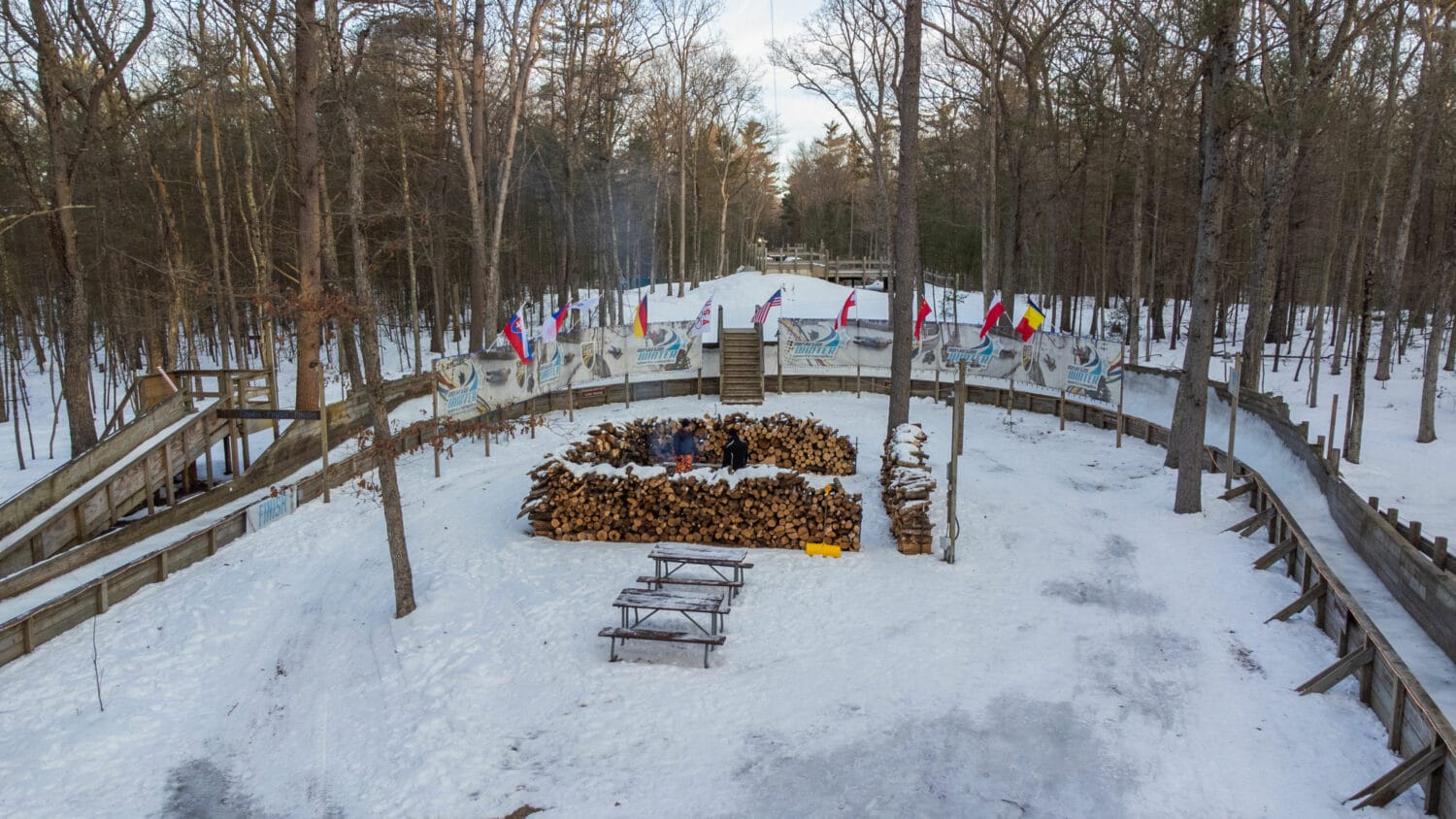 a winter luge track with a pile of firewood and multiple country flags on display