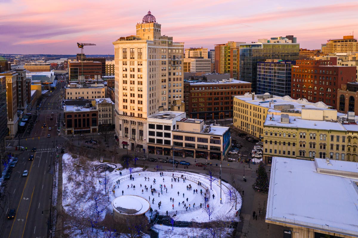 aerial view of a bustling grand rapids at dusk with a prominent historic building and an ice rink filled with skaters