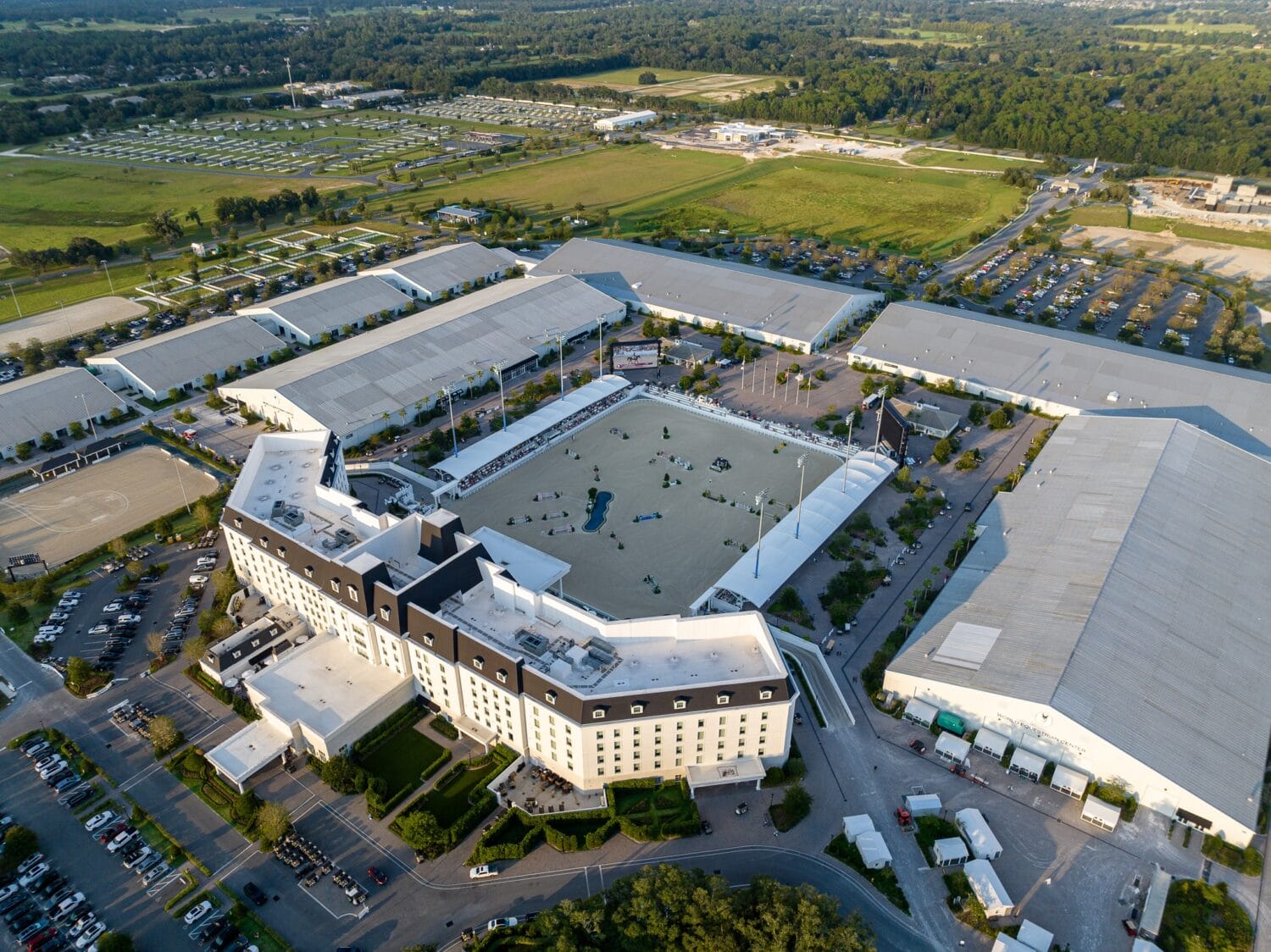 an aerial view of a large equestrian facility with multiple arenas extensive parking and a central hotel building