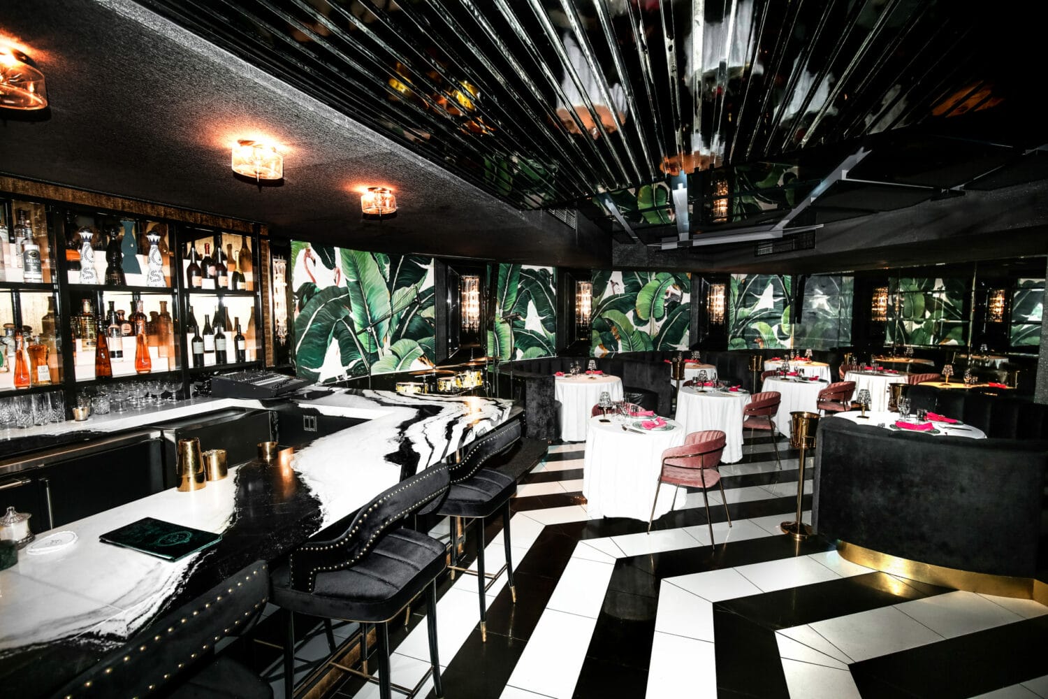 an elegant and modern interior of cash only supper club with mirrored ceiling tropical wallpaper and a blend of marble and black and white checkered floors