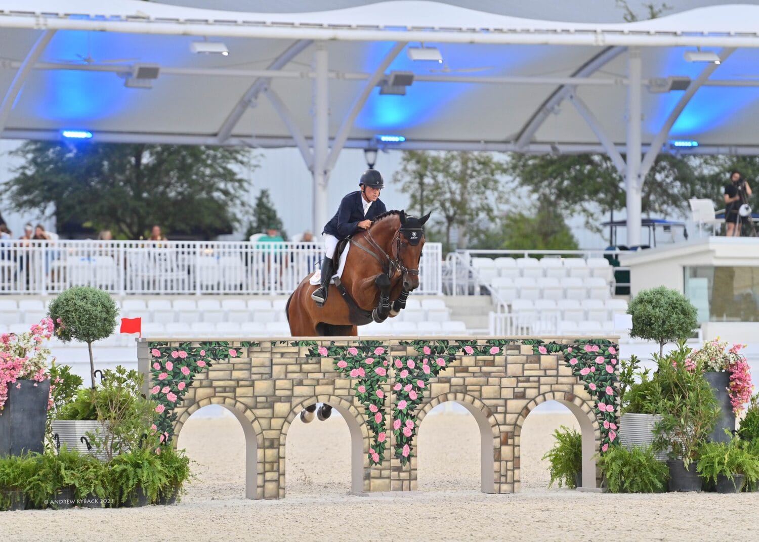 an equestrian rider jumping a horse over a brick wall obstacle