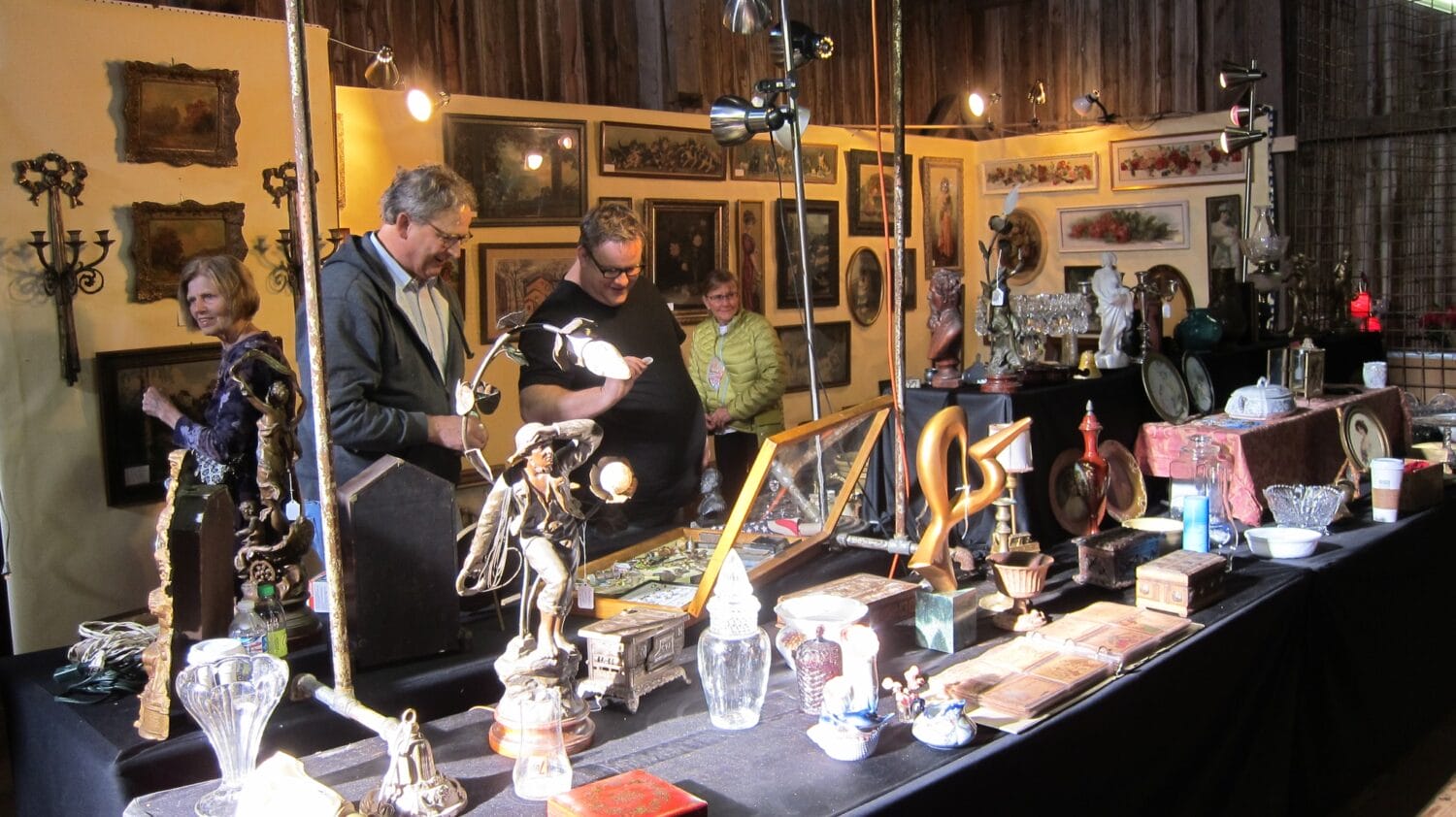 an indoor antique booth displaying an eclectic mix of vintage items with shoppers examining the treasures