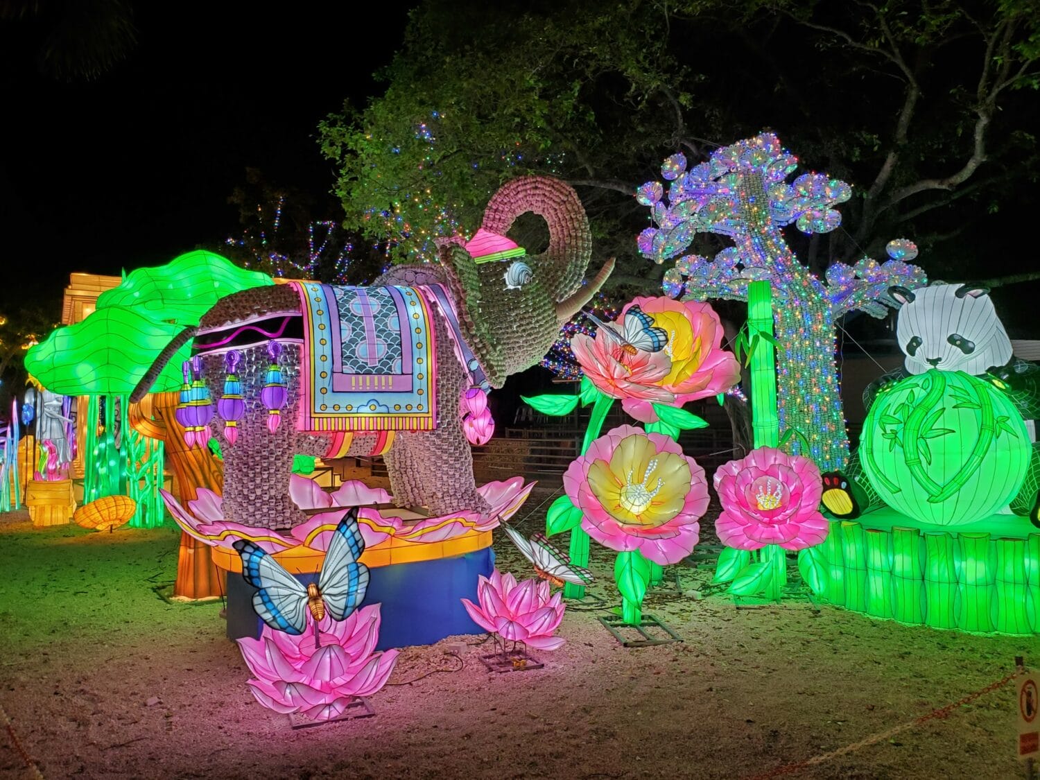 an ornate colorful elephant lantern surrounded by illuminated flowers and pandas in a light festival