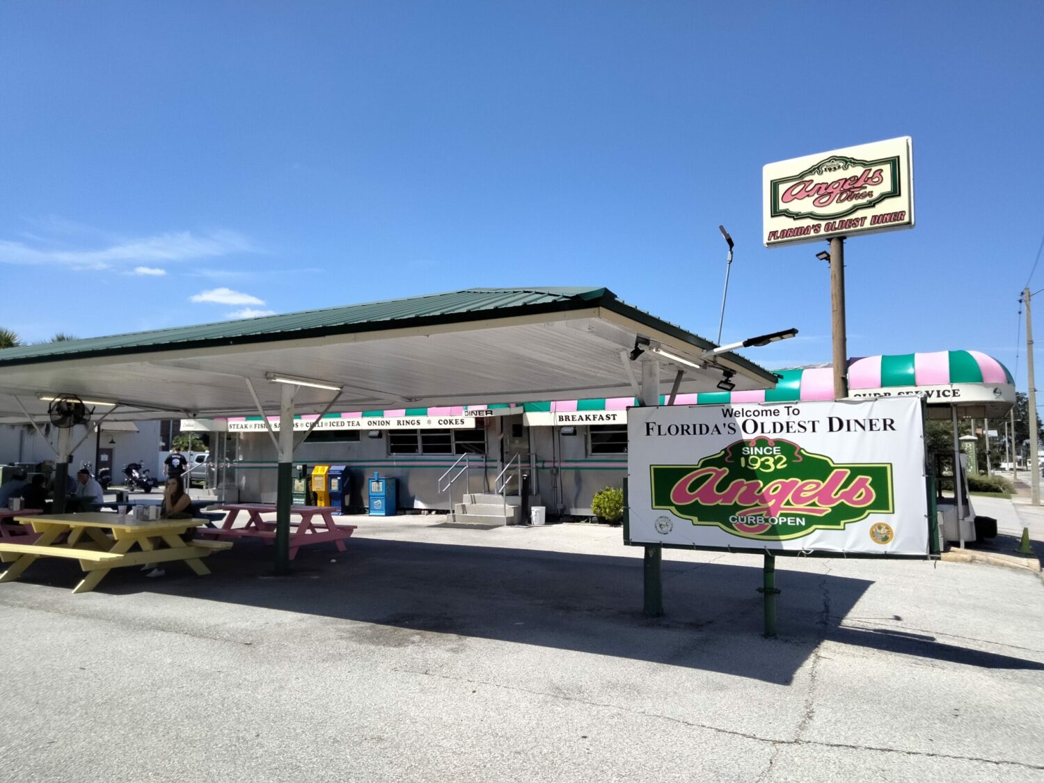 an outdoor view of angel's diner, proclaimed as florida's oldest diner, featuring picnic tables and a large sign.