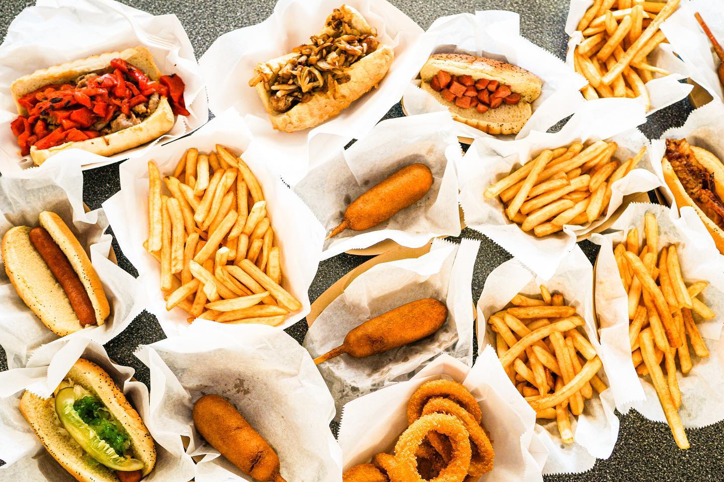 an overhead view of an assortment of hot dogs with various toppings and sides including french fries corn dogs and onion rings on a counter