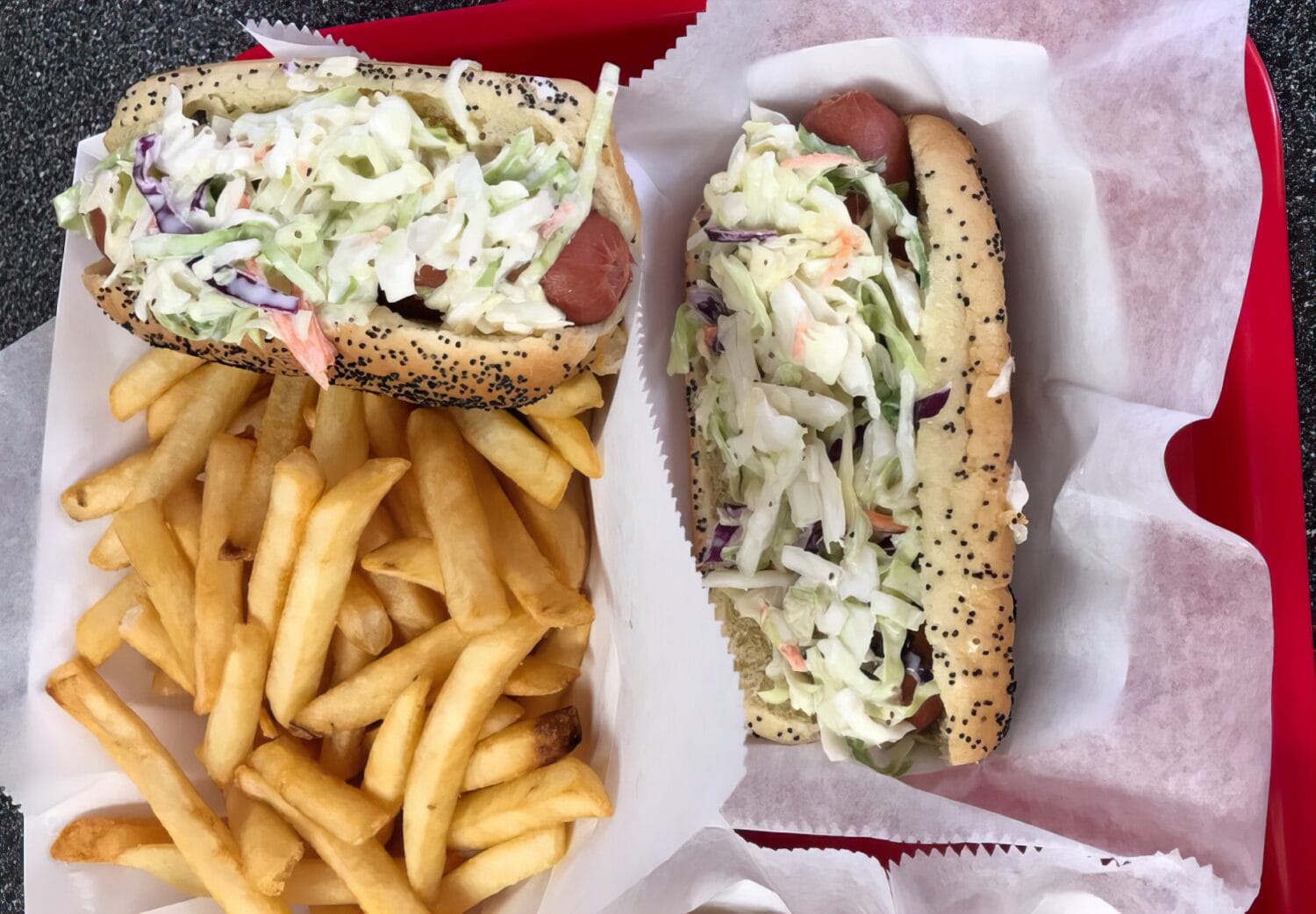 french fries and two hot dogs topped with coleslaw on a red cafeteria tray