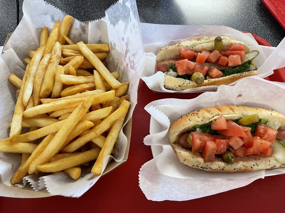 french fries and two hot dogs with fresh tomato and pickle toppings served in paper tray