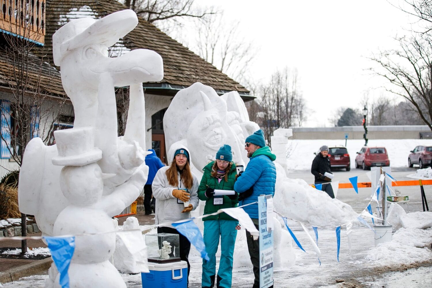 judges checking on detailed snow sculptures at a winter festival with onlookers and a street in the background