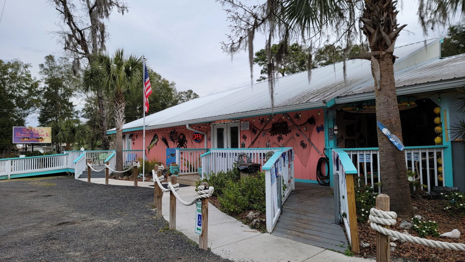 kathi's krab shack, a casual seafood restaurant, with a pink façade decorated with crab motifs and surrounded by lush palms and moss draped trees