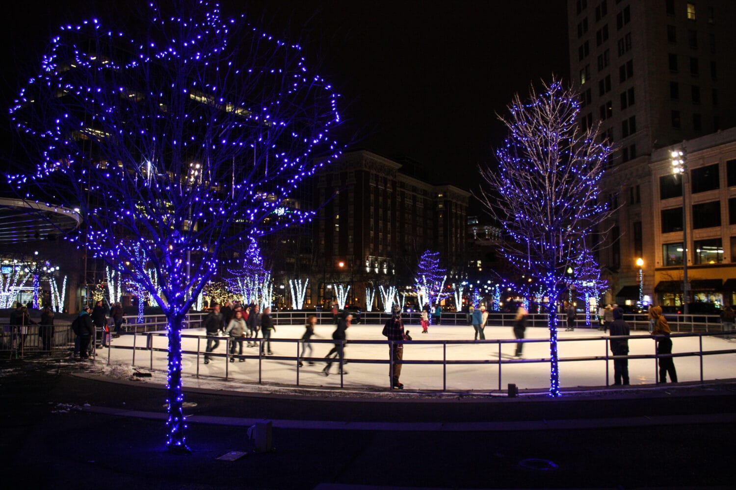 skaters enjoy a winter evening on rosa parks circle ice rink surrounded by trees adorned with bright blue lights