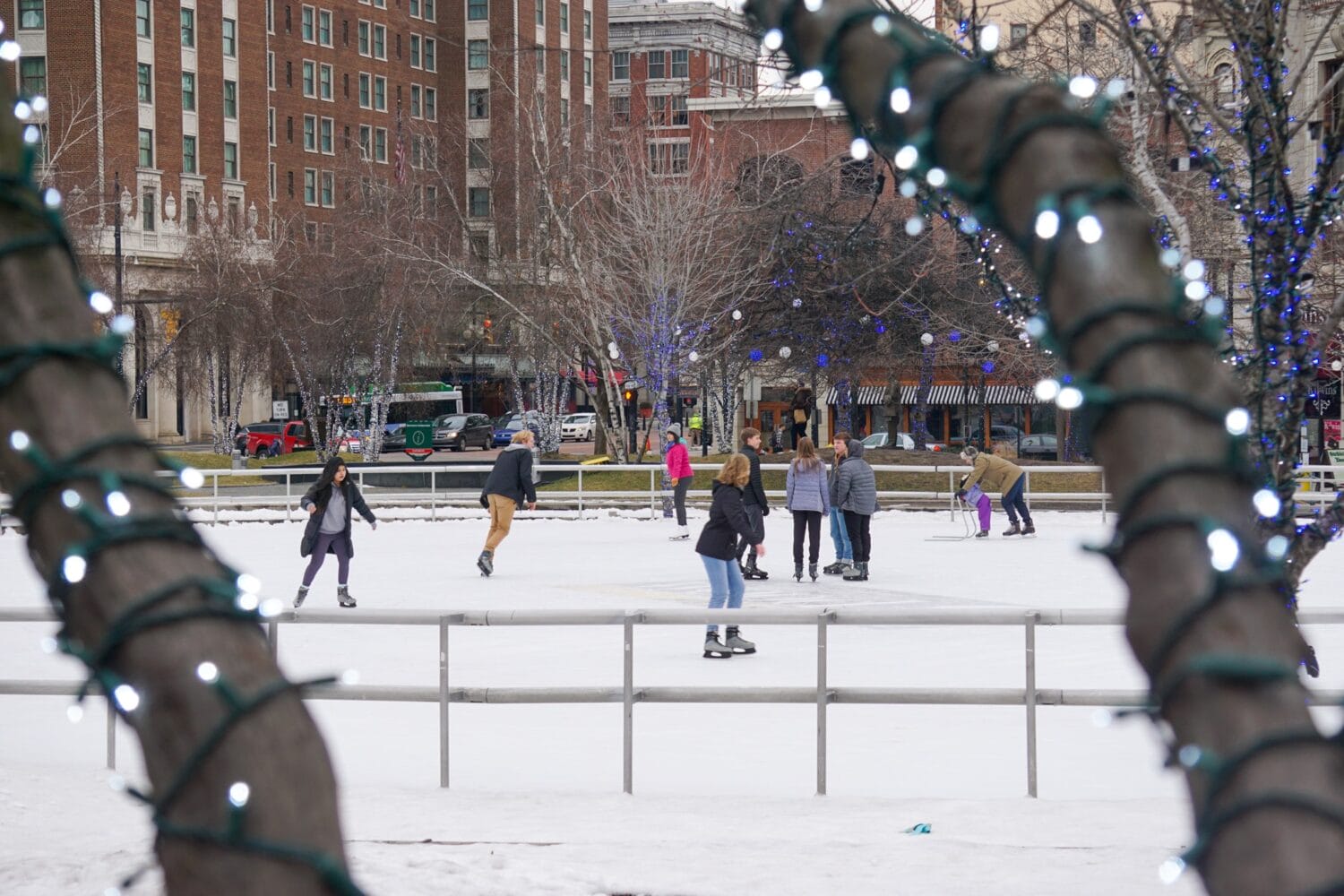 skaters of various ages enjoy a winter day on an ice rink in rosa parks circle with urban buildings in the backdrop