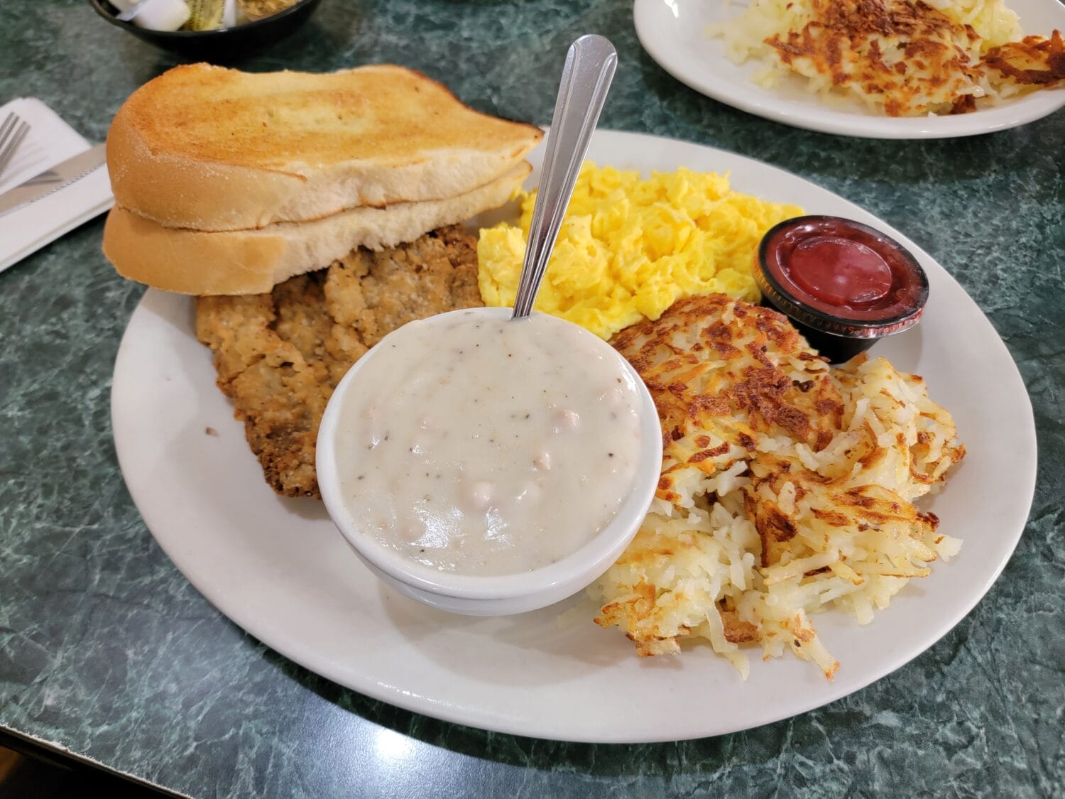 The diner's breakfast plate with a generous serving of fried chicken cutlet, eggs, hash browns, gravy, and toast