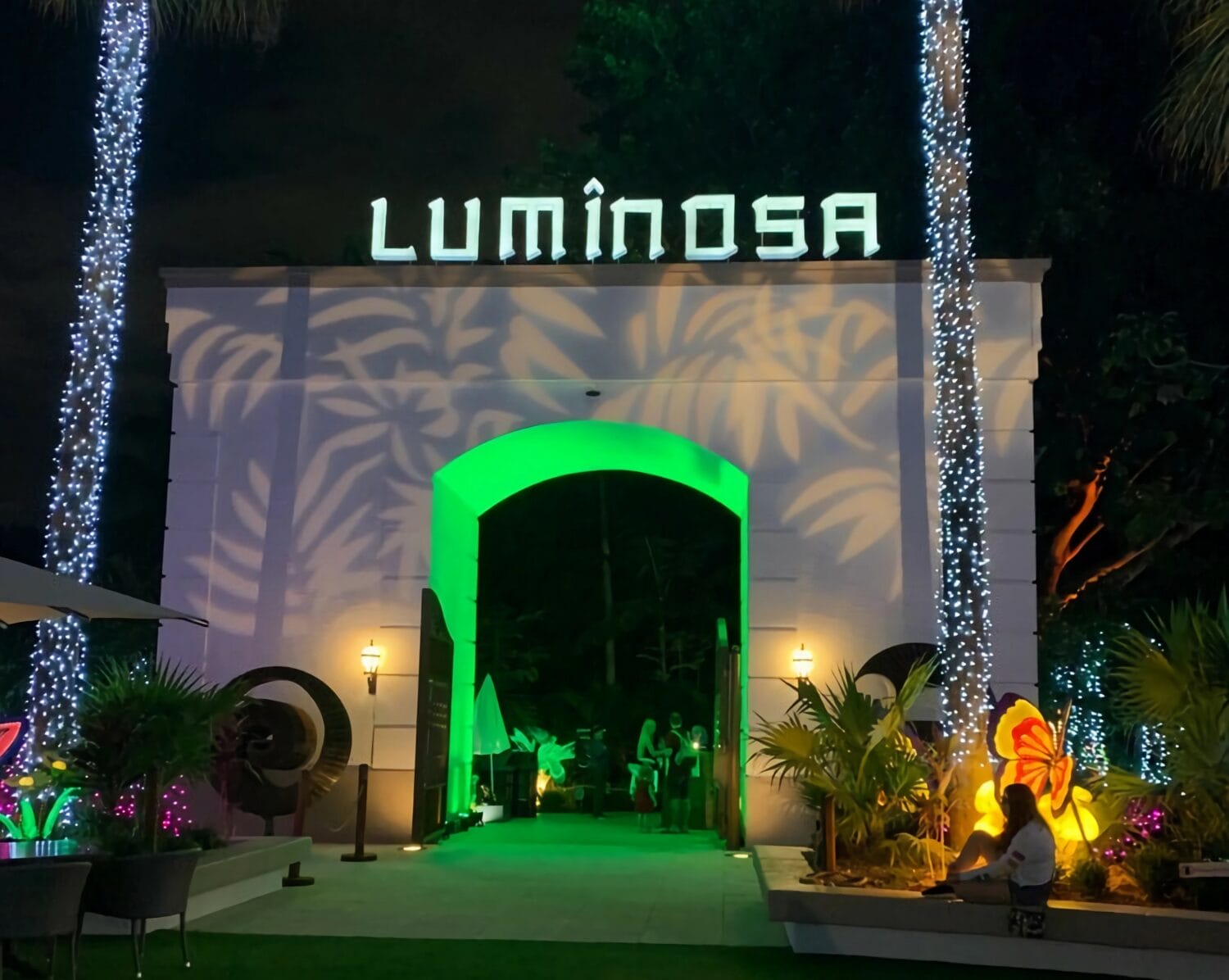 the entrance to luminosa festively adorned with twinkling lights and tropical illuminated sculptures under a night sky