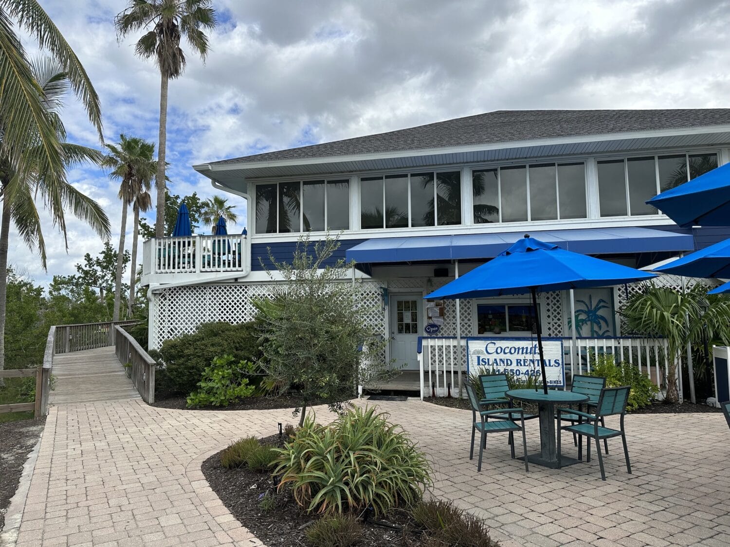 the exterior of the restaurant with blue umbrellas and tropical palm trees
